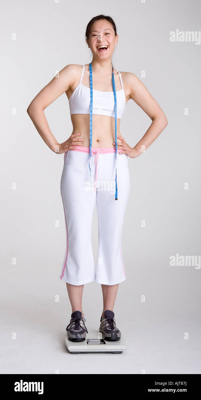 Portrait of a young woman standing on a weighing scale and laughing ...