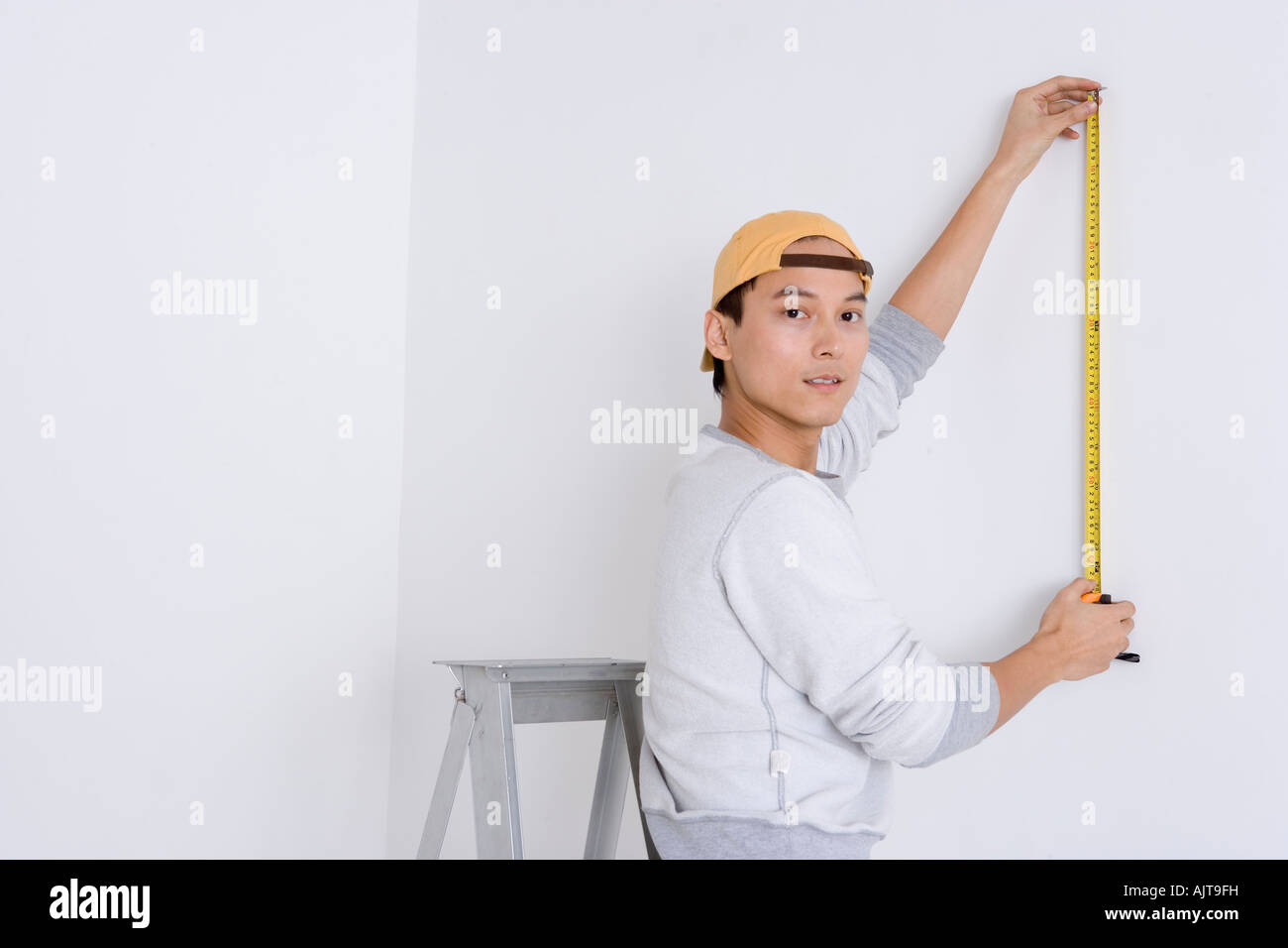 Portrait of a young man standing and measuring a wall with a tape ...
