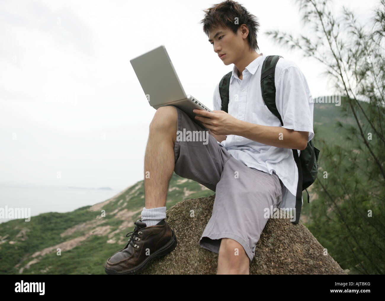 Young man sitting on a rock and using a laptop Stock Photo - Alamy