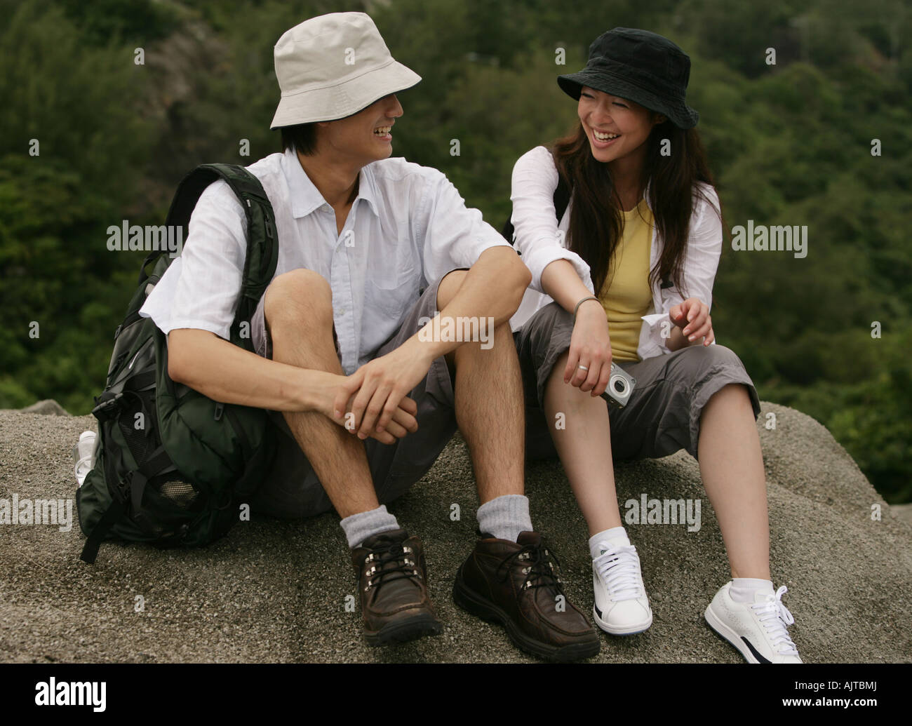 Young couple sitting on a rock and laughing Stock Photo - Alamy