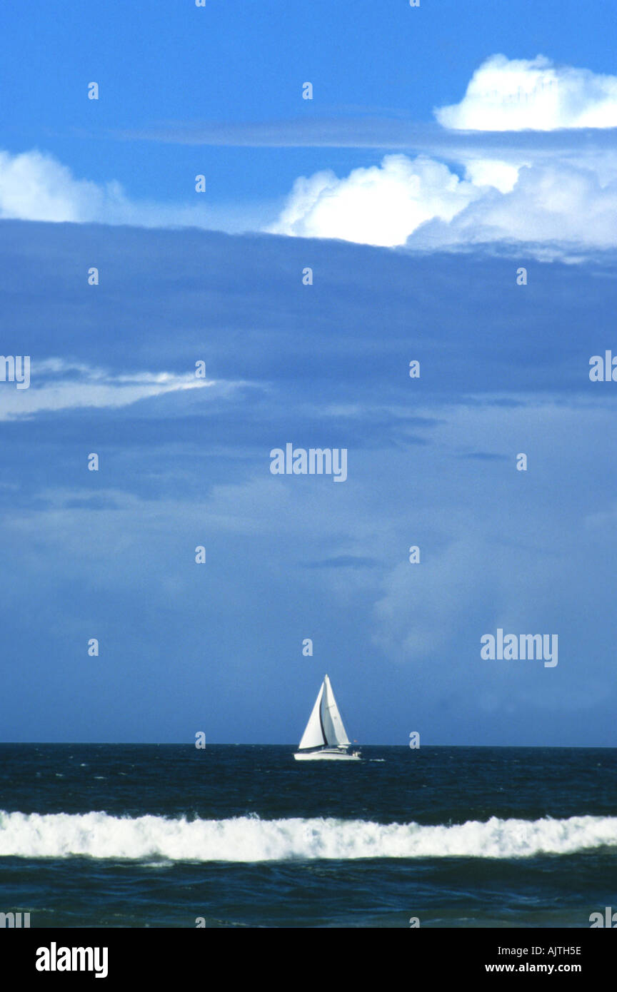 Sailboat in the distance under massive clouds and above a breaking wave ...