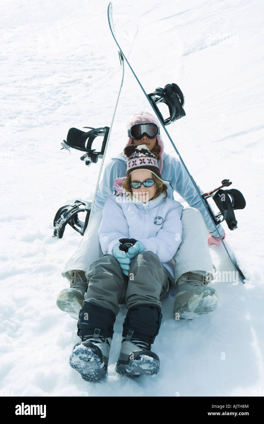Two young skiers sitting under skis together, smiling at camera ...