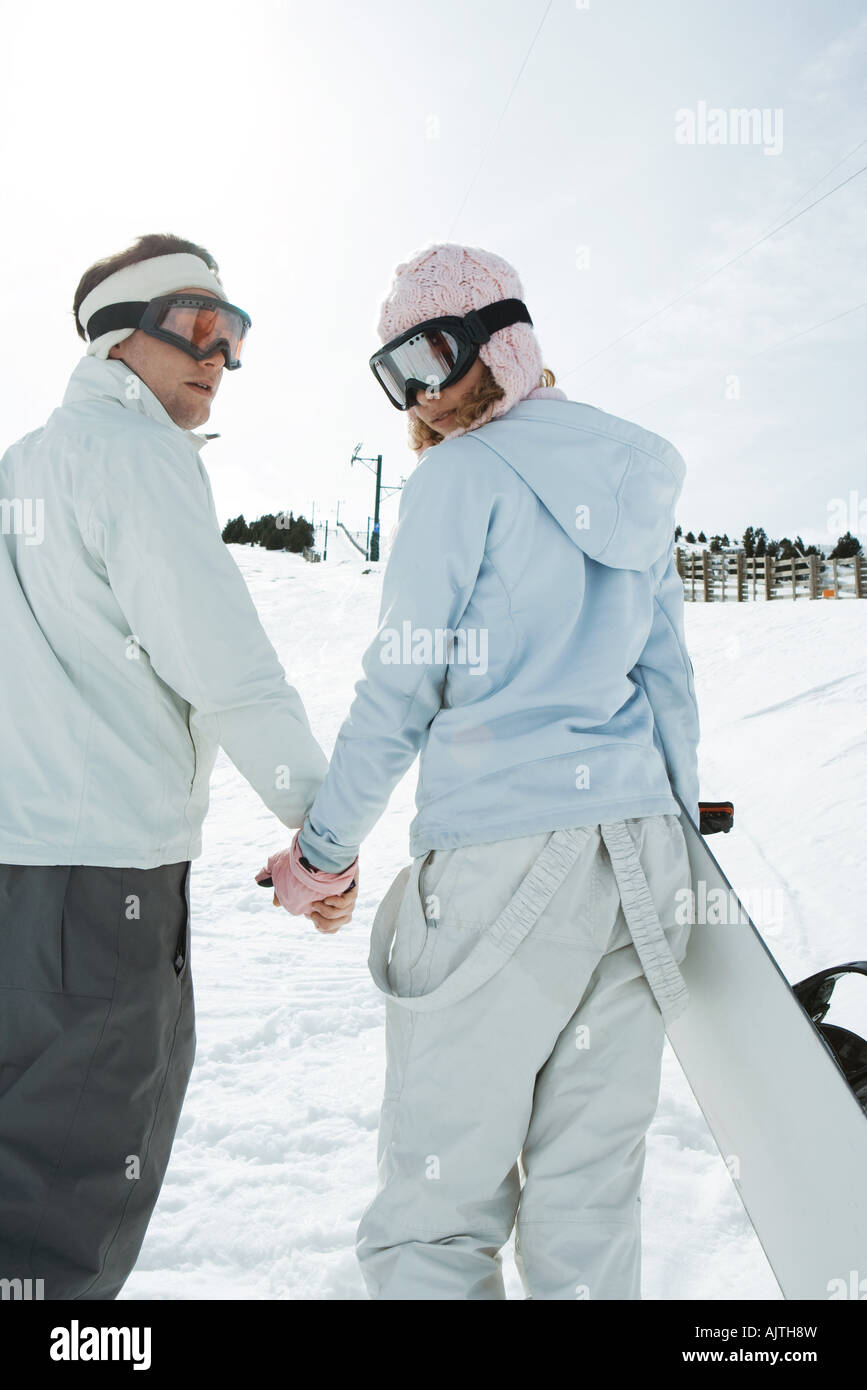 Two young friends walking, holding hands, looking over shoulders, one ...