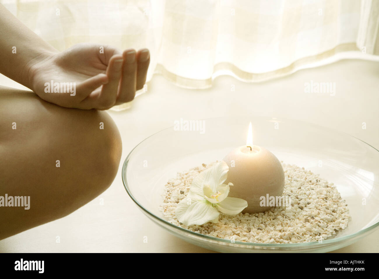 Female sitting in lotus position next to candle, cropped view of hand ...