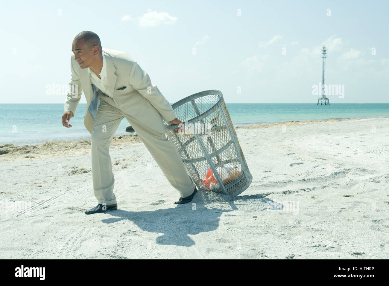 Man in suit pulling garbage can across sunny beach, full length Stock ...