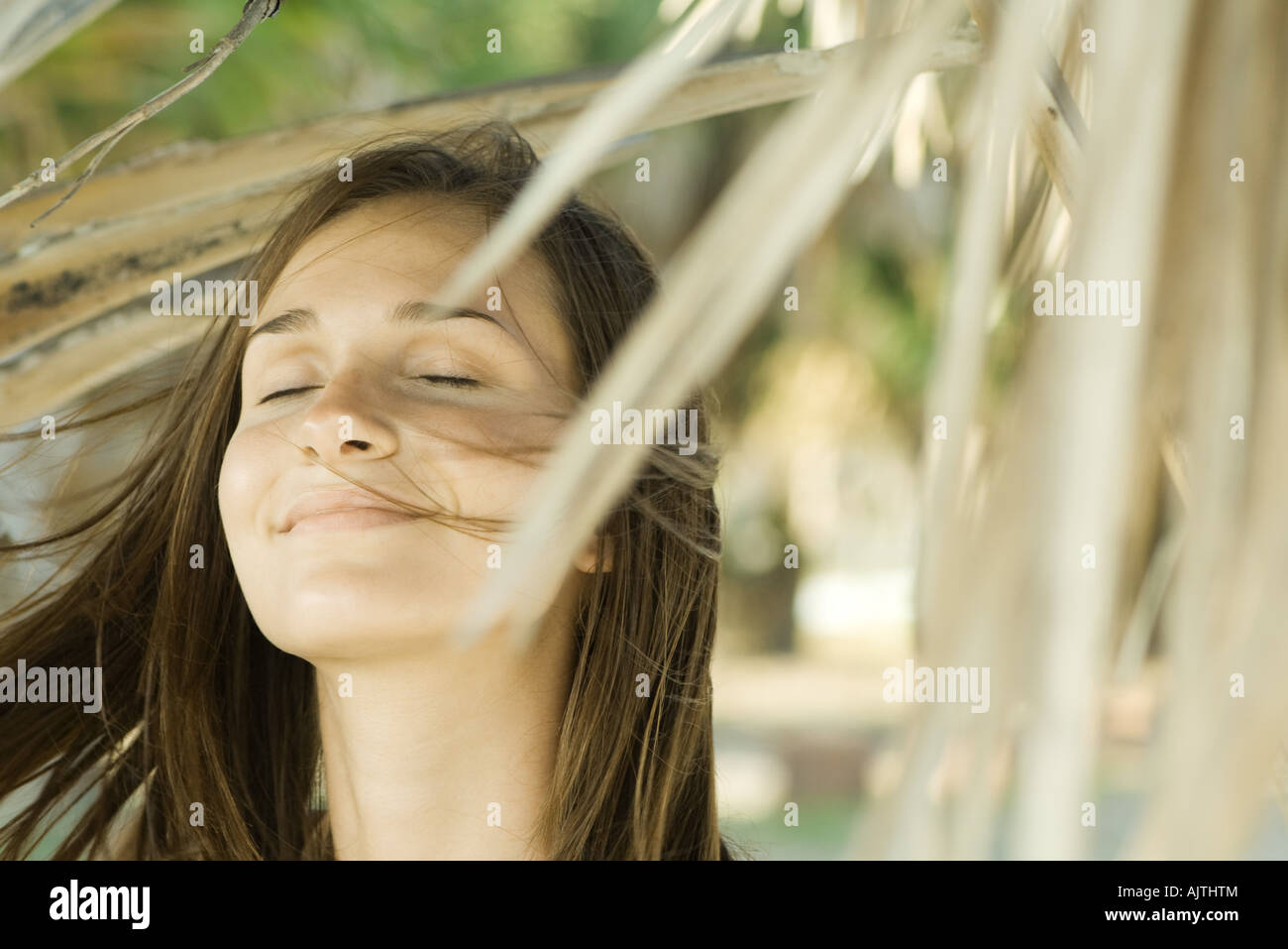Woman surrounded by dry foliage, eyes closed, hair blowing in wind ...