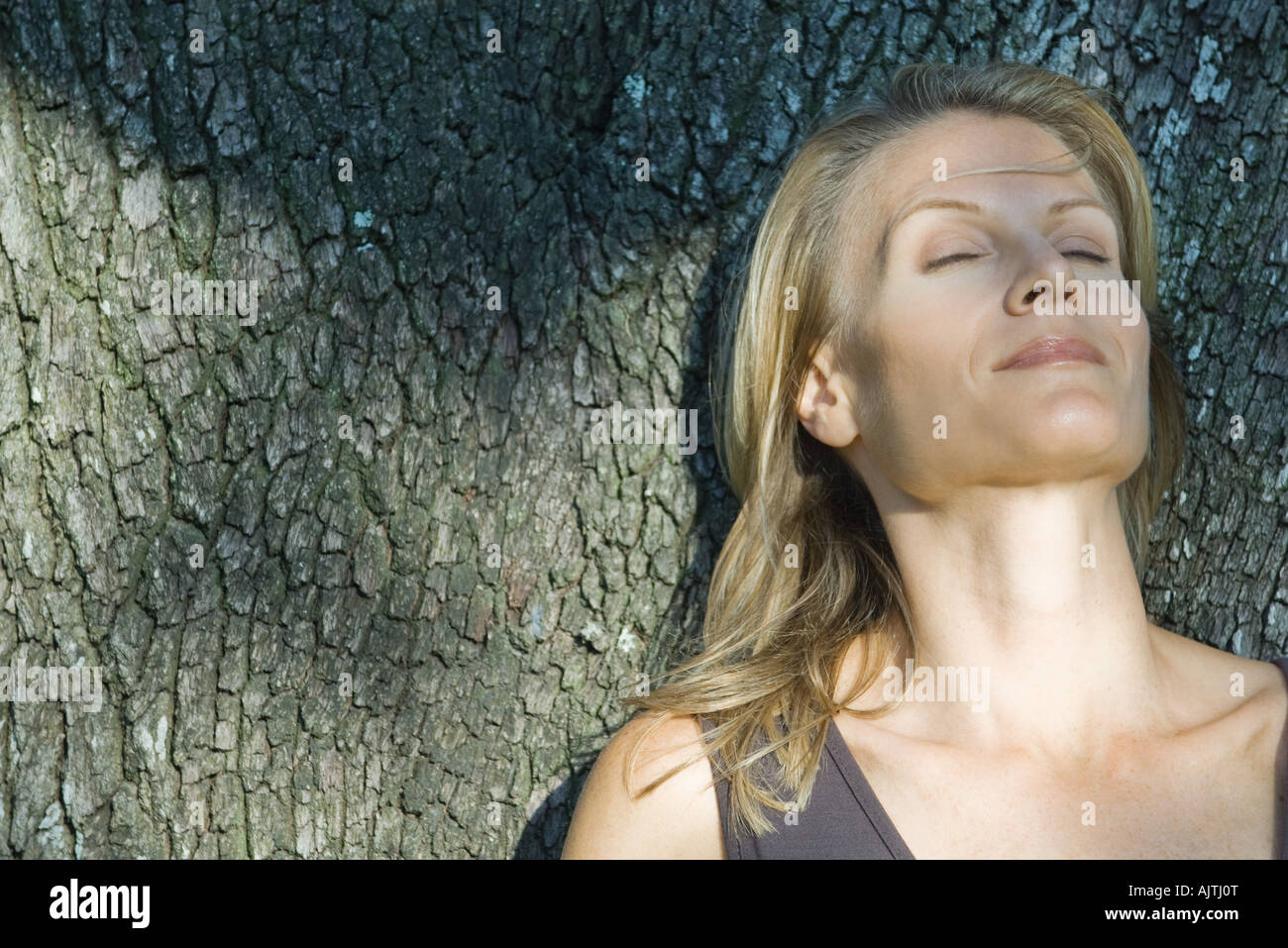 Woman leaning back against tree trunk, head and shoulders Stock Photo ...