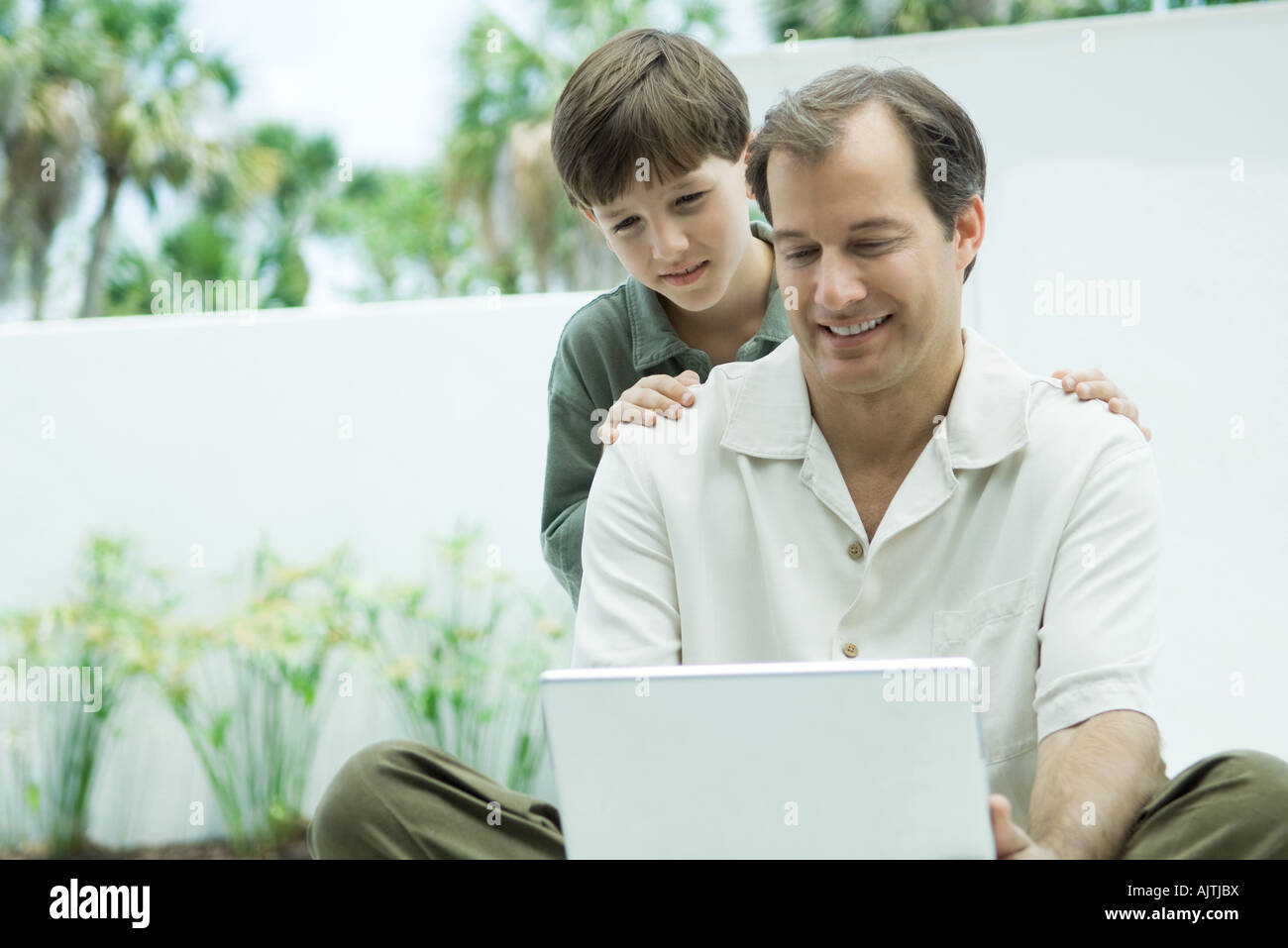 Man using laptop computer, son looking over his shoulder Stock Photo ...