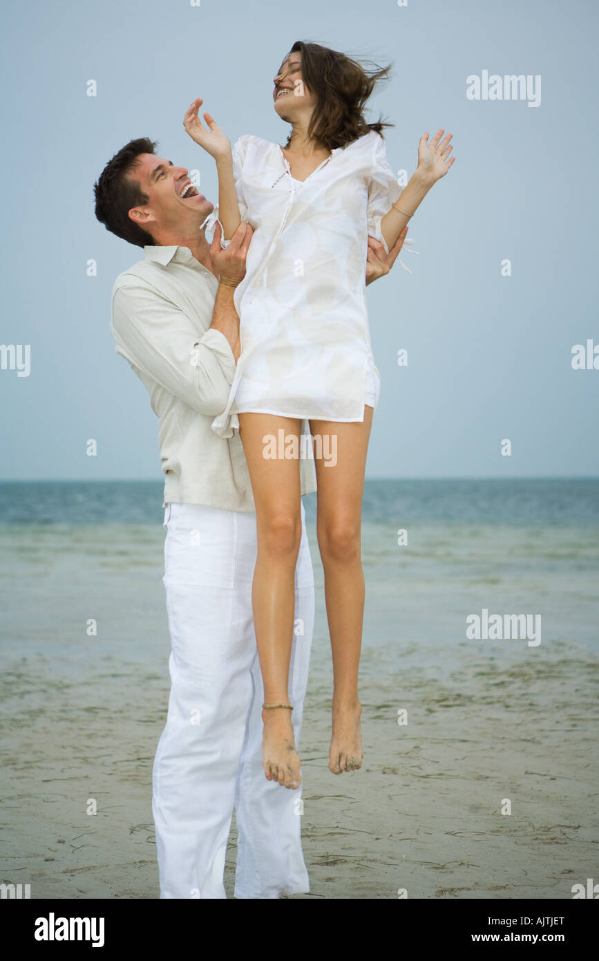 On beach, man holding young female companion up in air, full length ...