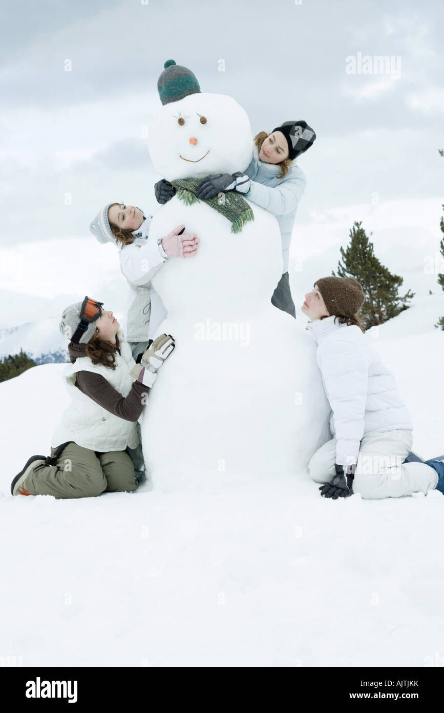 Young female friends grouped around snowman Stock Photo - Alamy