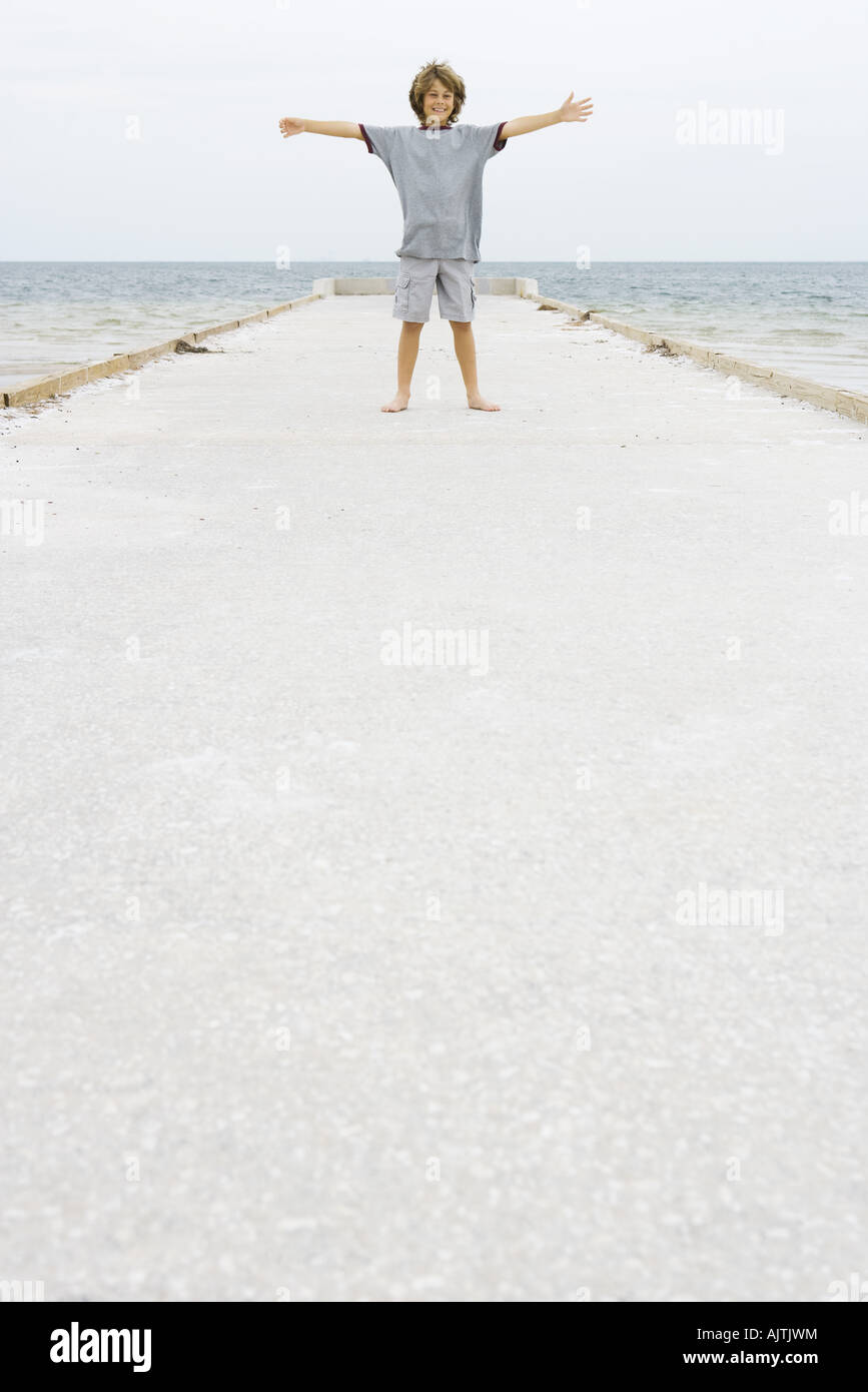 Boy standing on pier with arms out, smiling at camera, full length ...