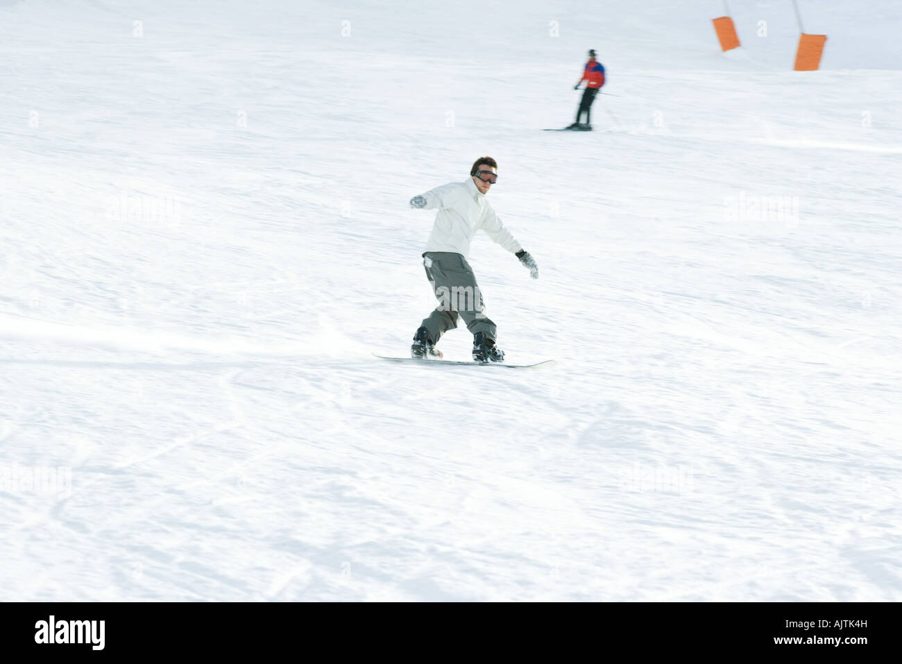 Young man snowboarding on ski slope, full length, skier in background ...