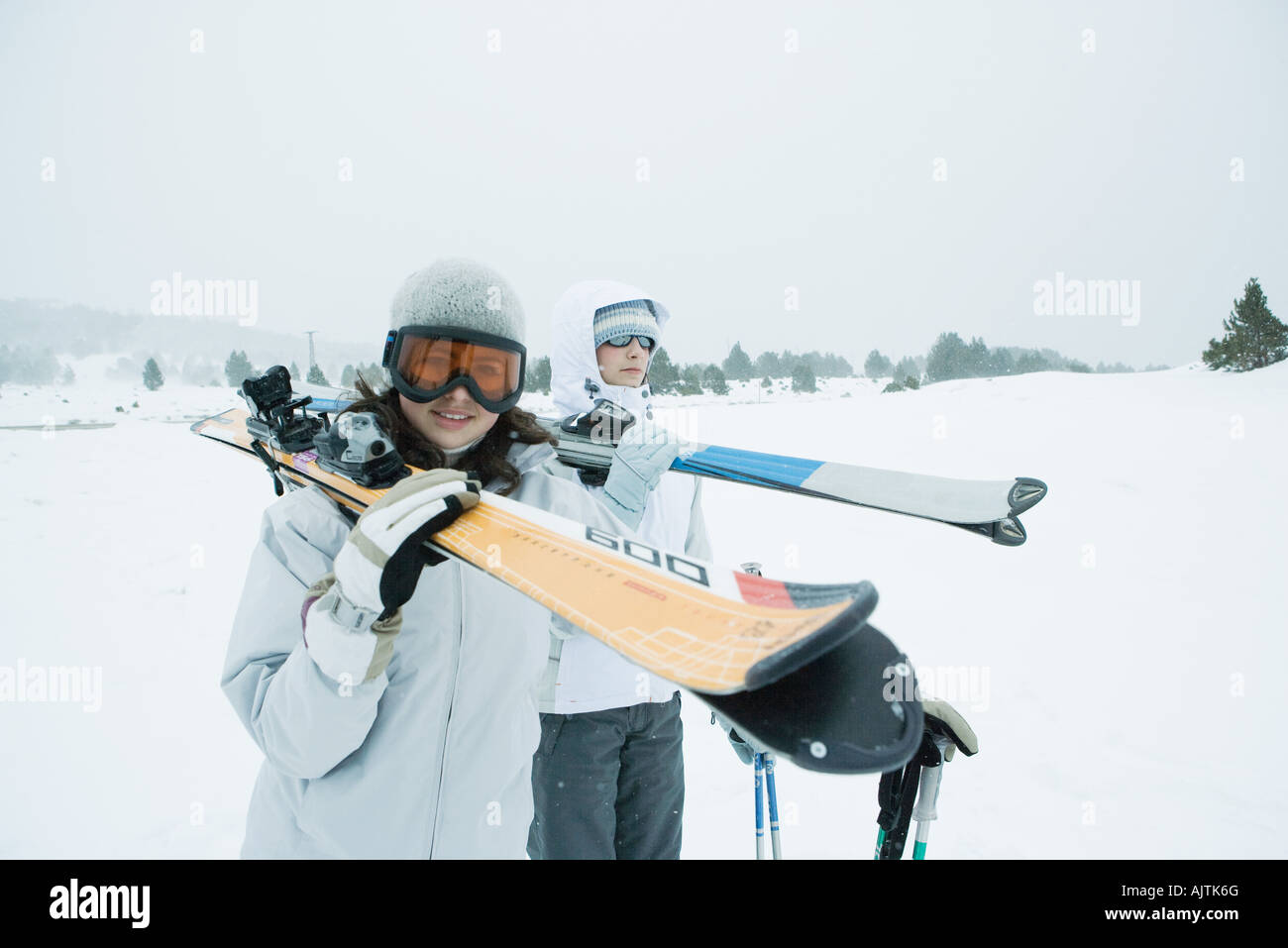 Two young skiers walking together, carrying skis on shoulders, one ...