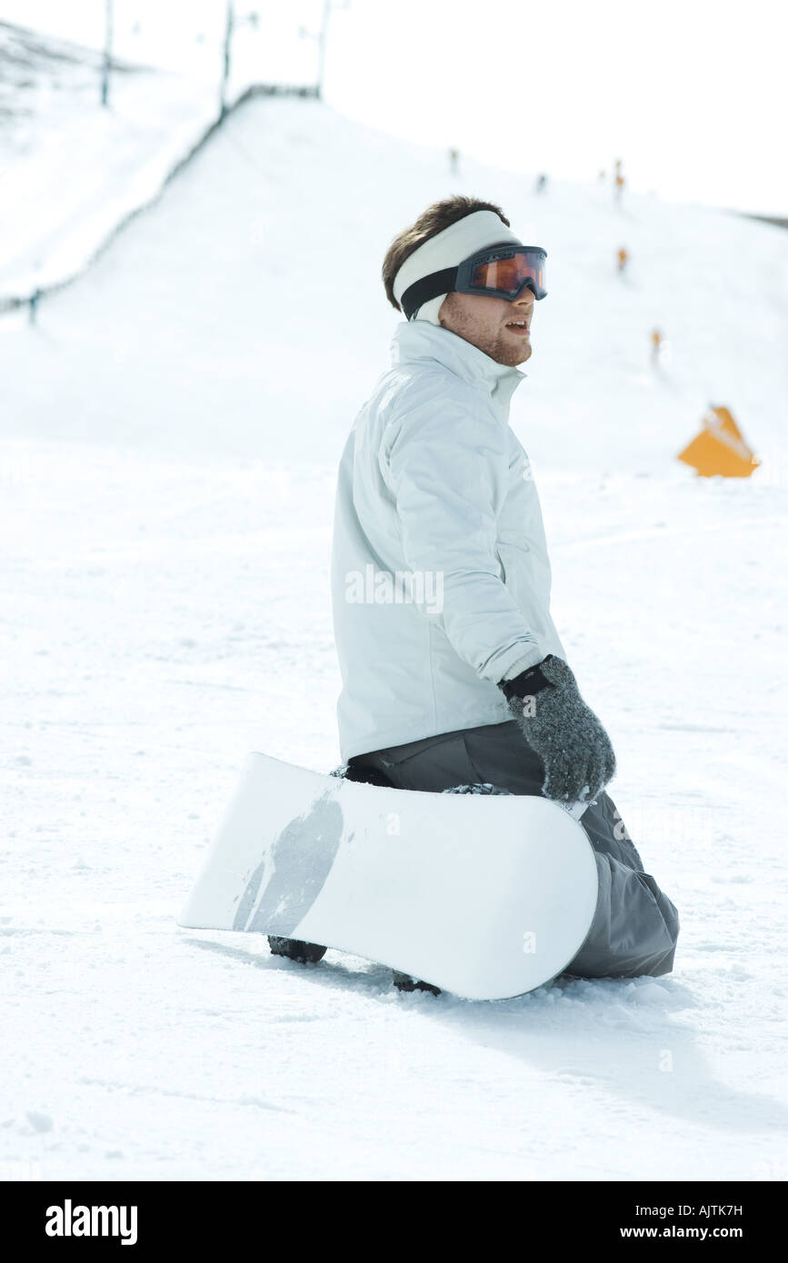 Young snowboarder kneeling on ski slope, looking away, side view Stock ...