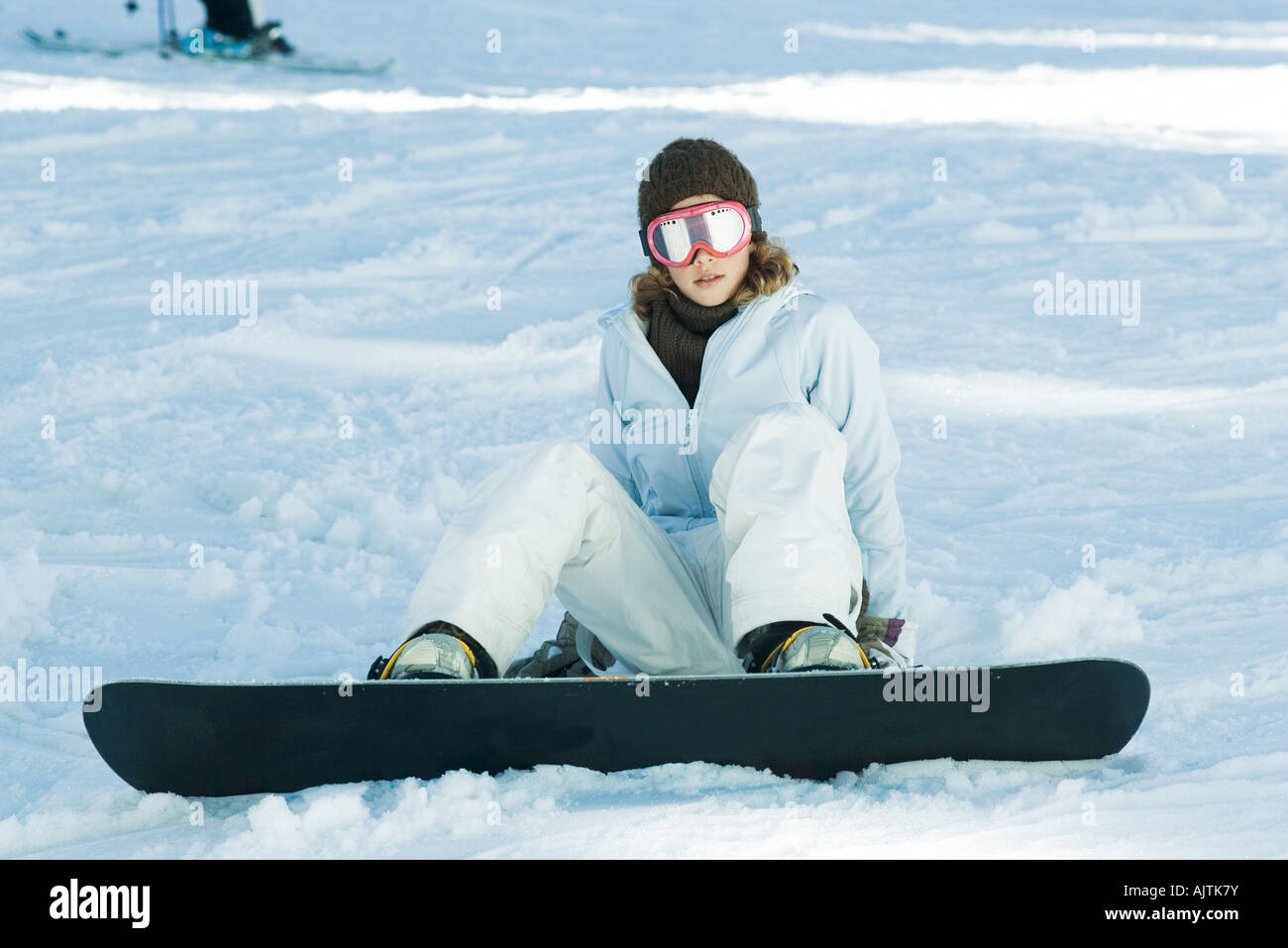 Young snowboarder sitting on the ground, looking at camera, full length ...