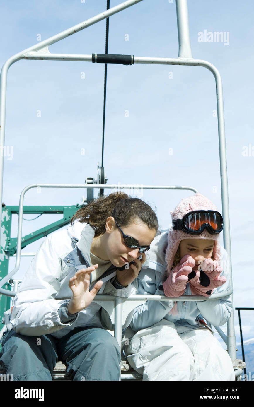 Two teenage girls sitting on chair lift together, looking over side ...