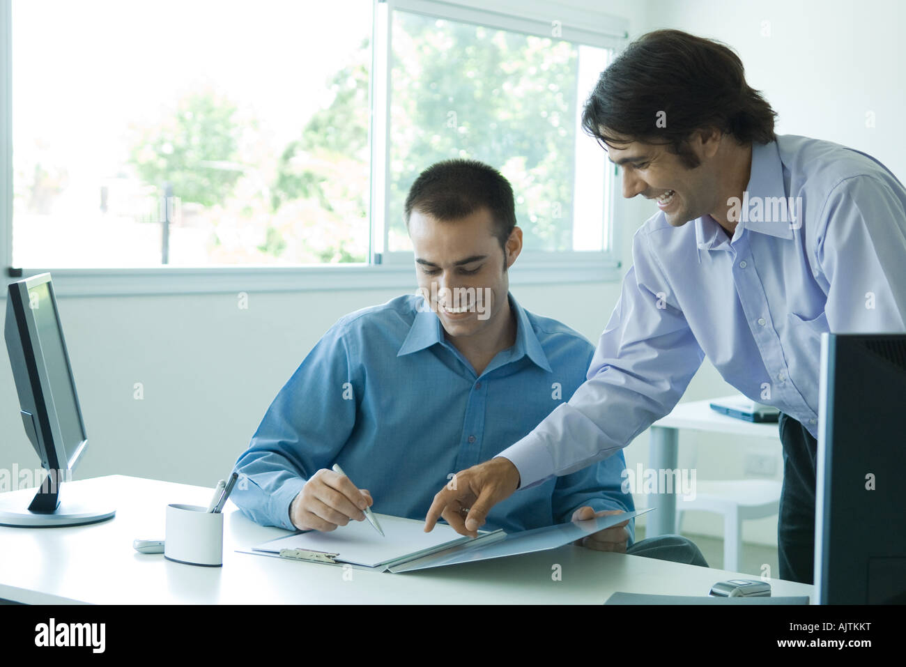 Two young businessmen looking at document together, laughing Stock ...