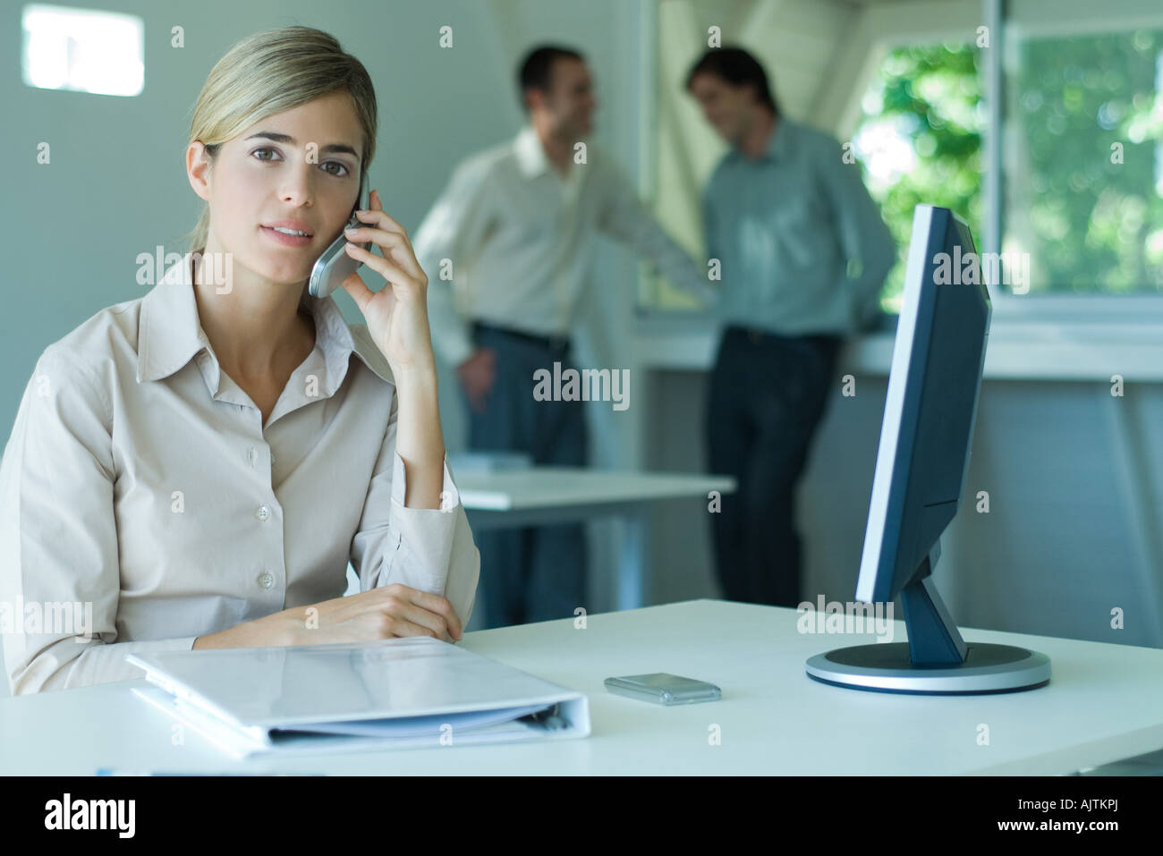 Woman sitting at desk, using cell phone, male colleagues standing in ...
