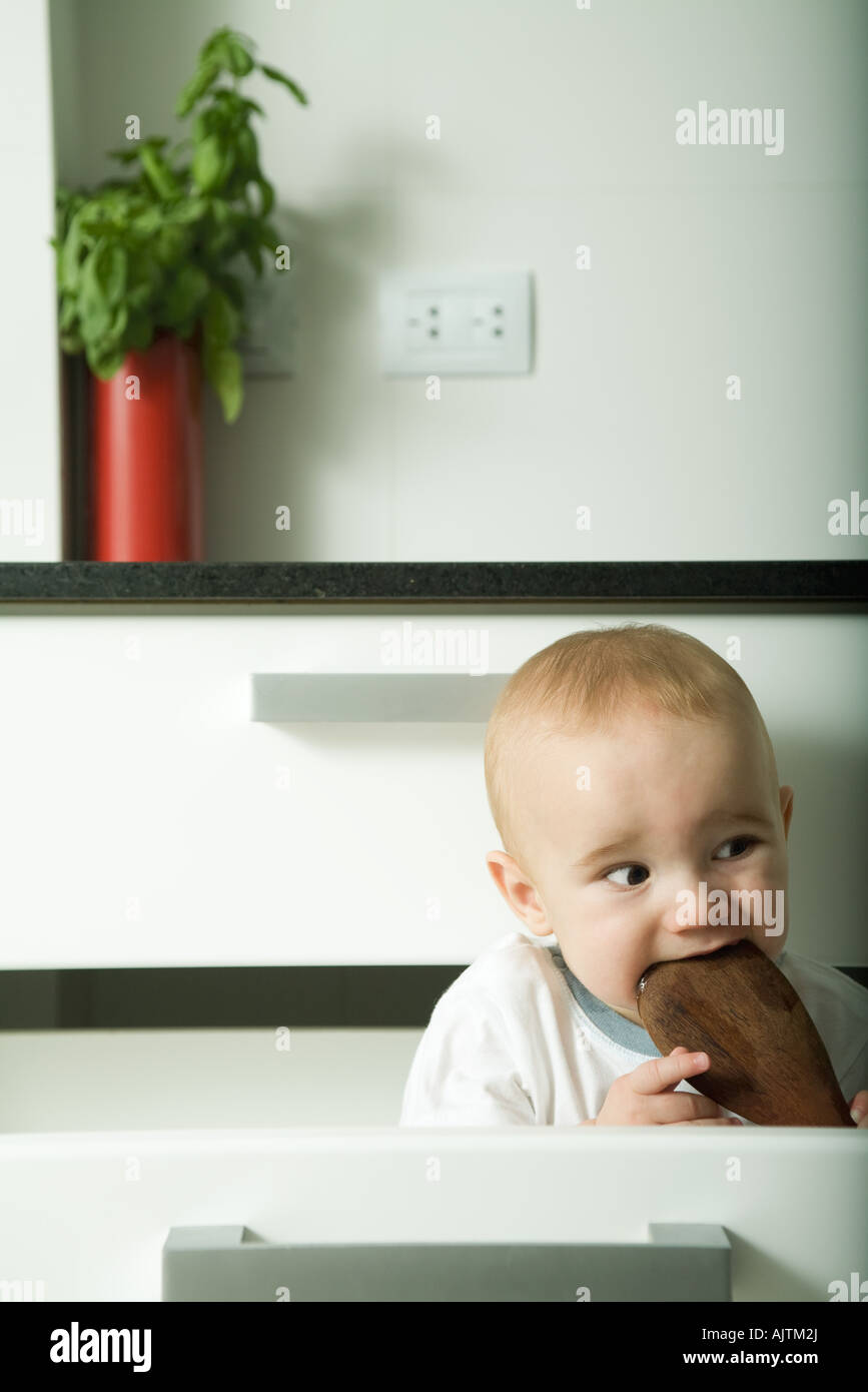 Baby in drawer, biting on wooden spoon, making funny face Stock Photo ...