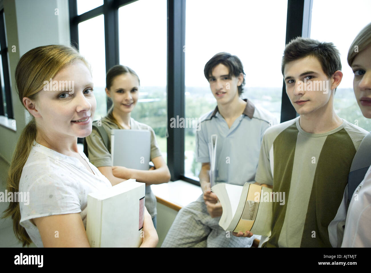 Group of college students standing around, holding books and binders ...