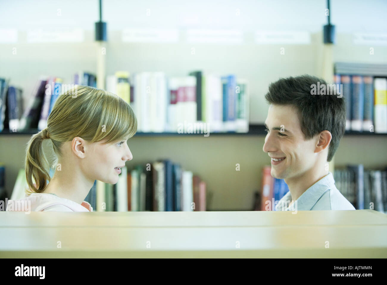 Male and female college students face to face in library, smiling at ...