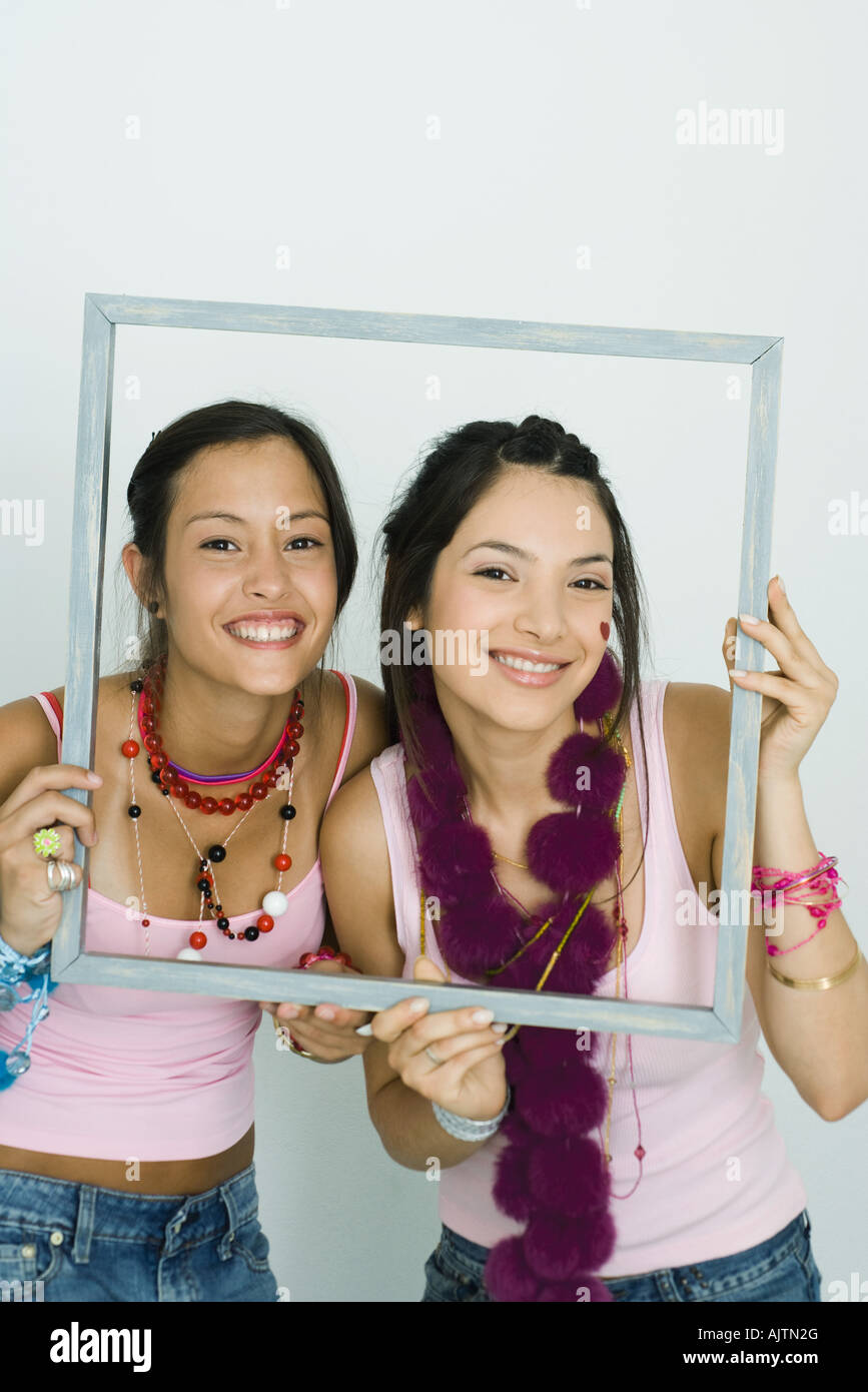 Two young friends holding up frame together, smiling at camera ...