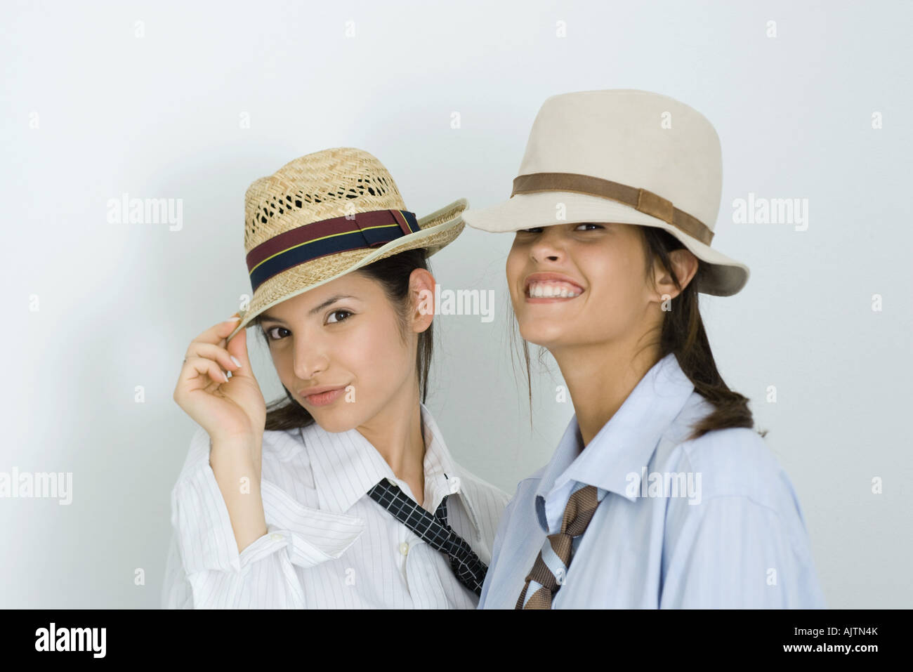 Two young female friends wearing hats and ties, smiling at camera ...
