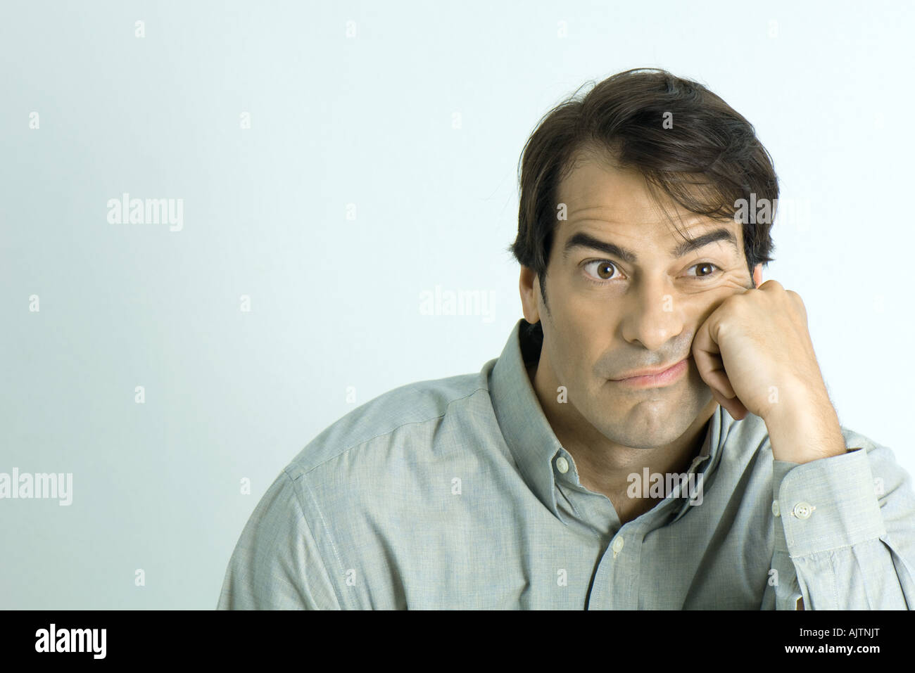 Man leaning face against hand, looking grumpy Stock Photo - Alamy