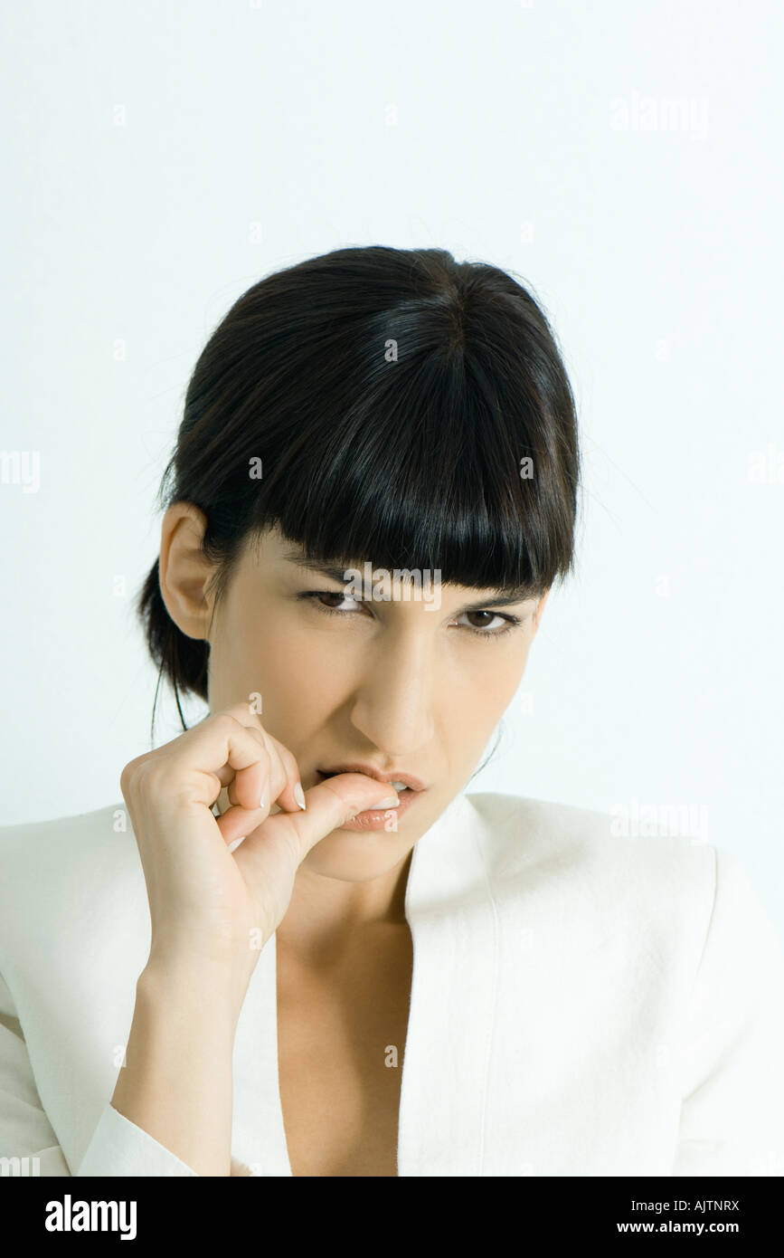 Well-dressed young businesswoman biting thumb, looking at camera ...