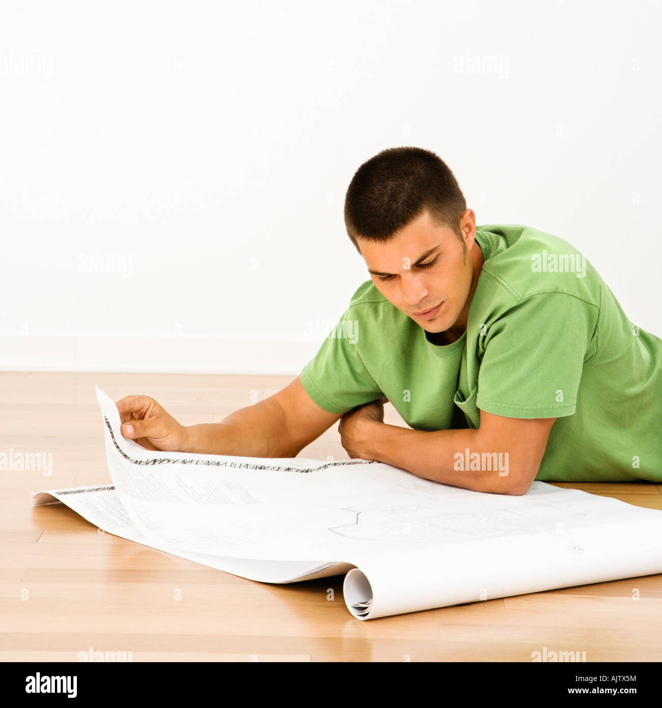 Attractive man lying on floor in home reading house plans Stock Photo ...
