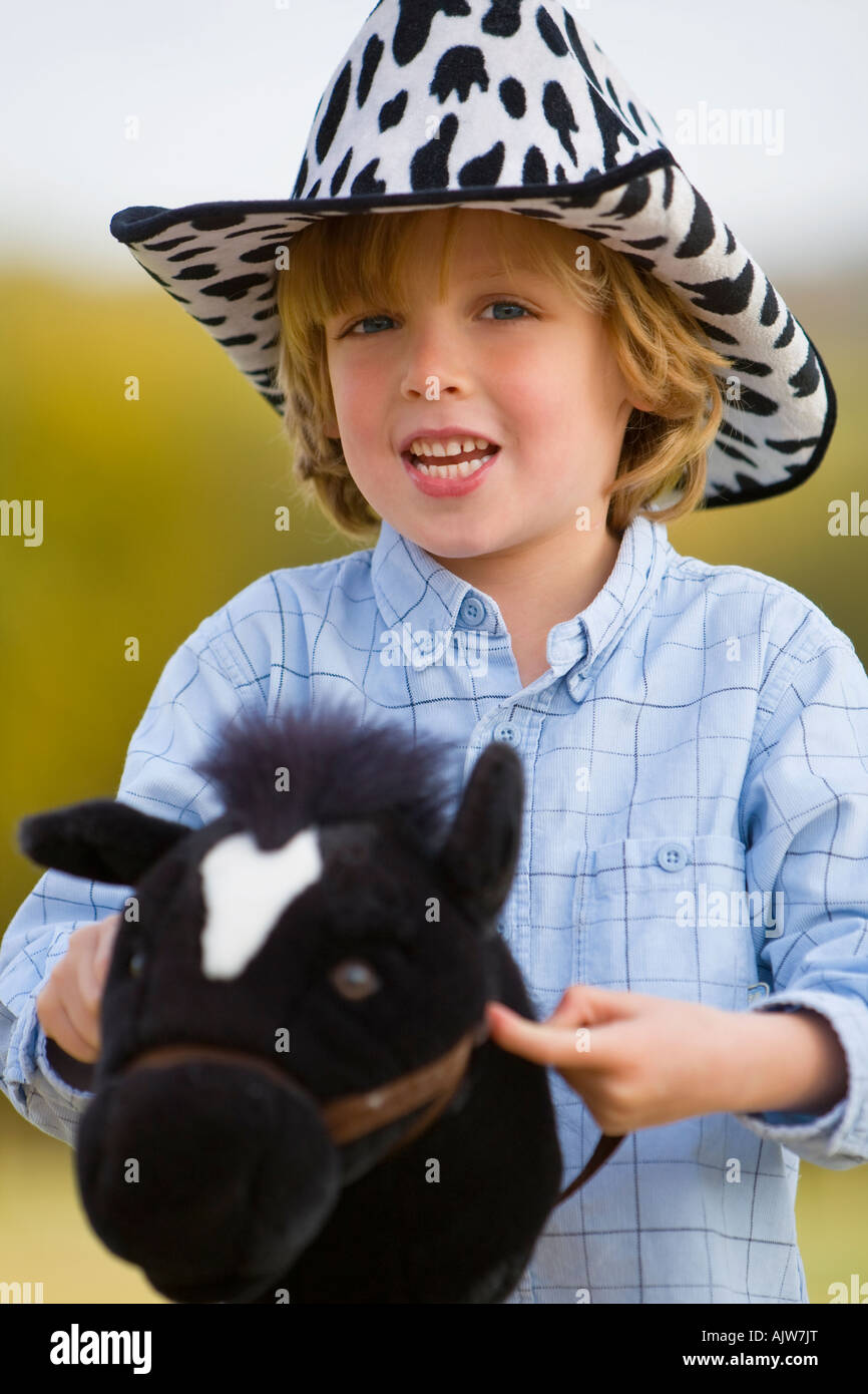 A young boy having fun riding a hobby horse and dressed as a cowboy ...