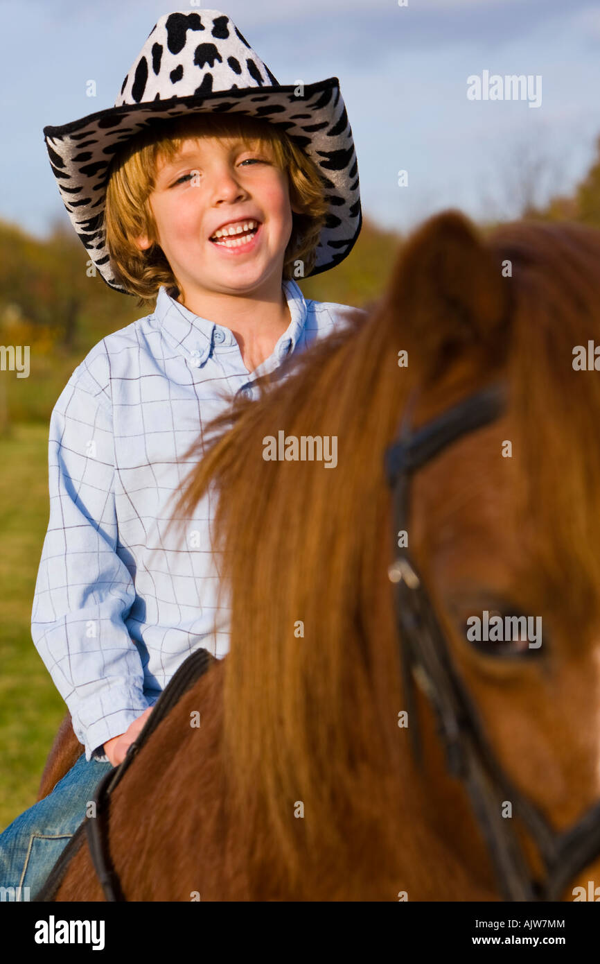 A young boy having fun riding a pony and dressed as a cowboy Stock ...