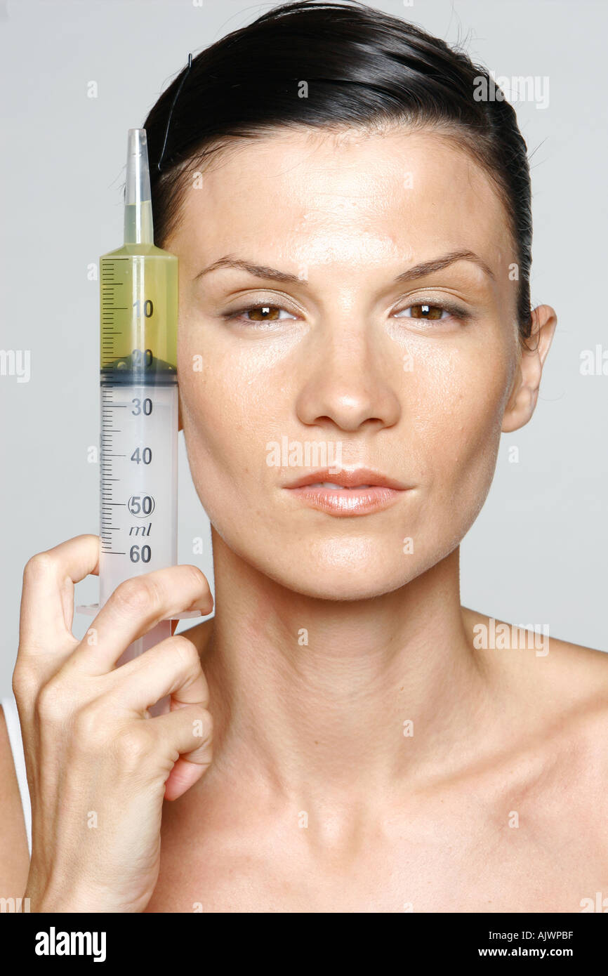 Woman holding syringe by her face, looking at camera Stock Photo - Alamy