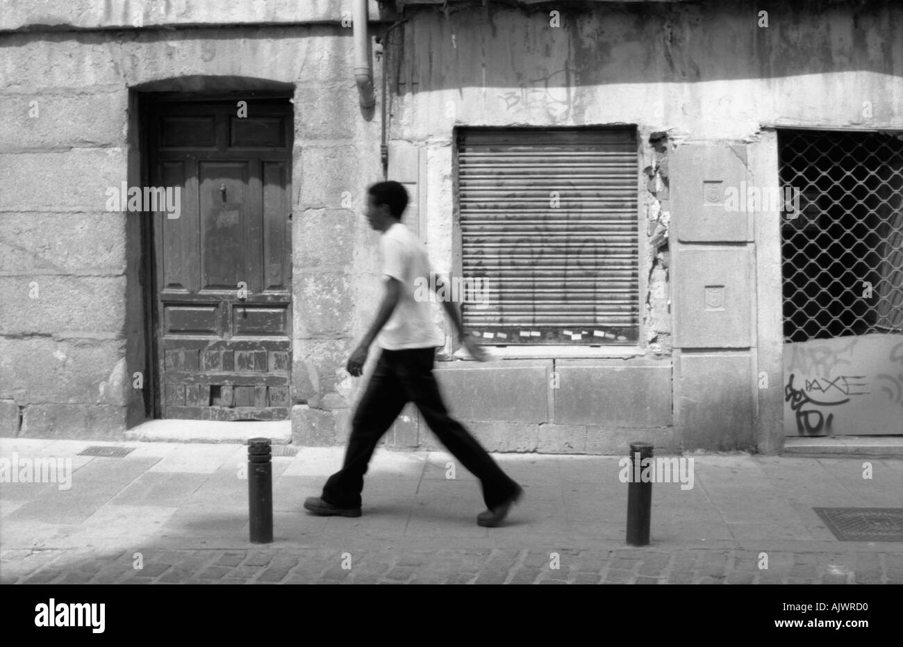 Young man walking past neglected derelict crumbling run down buildings ...