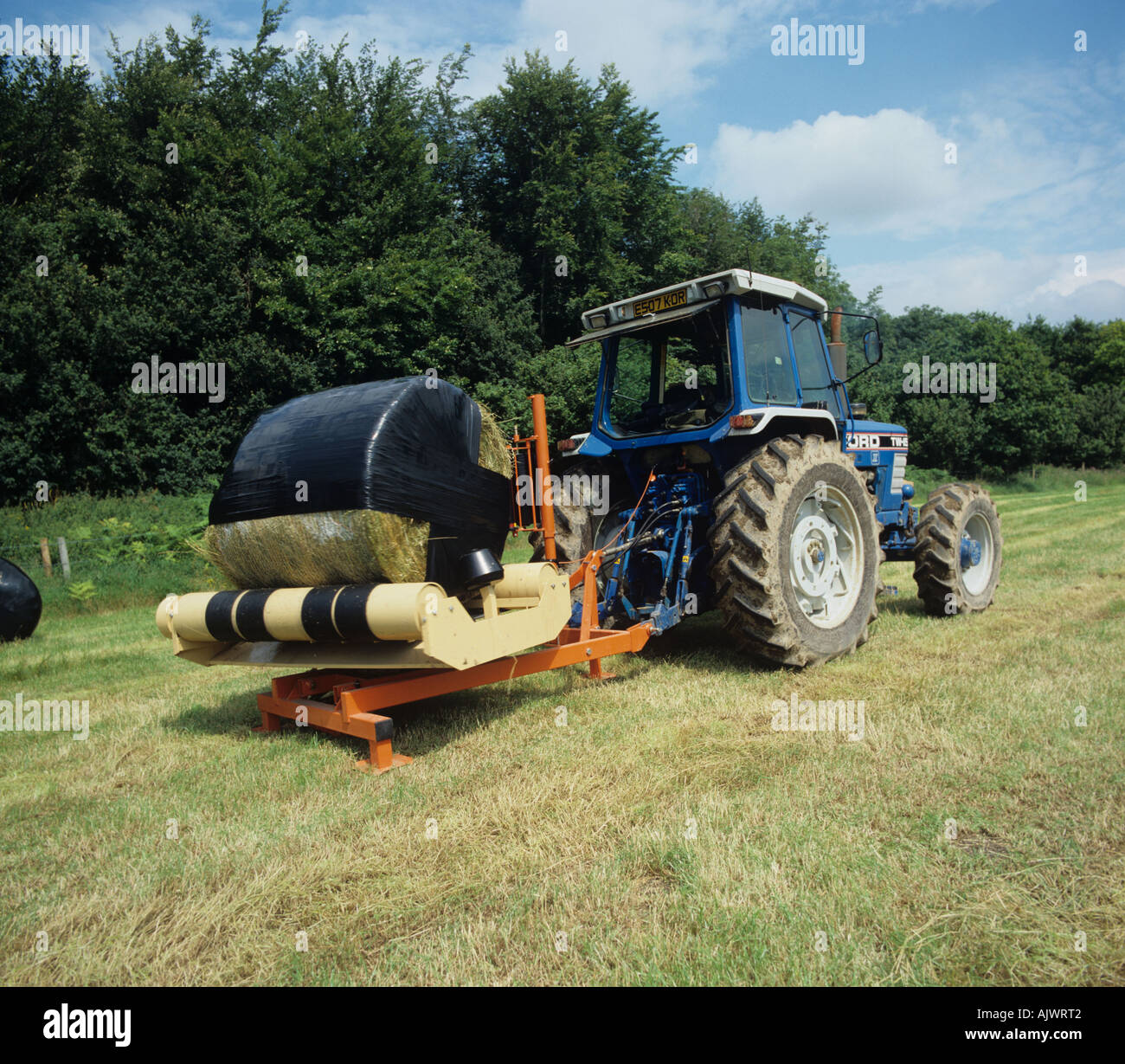Tractor rotating platform being used to wrap grass silage bale in black ...