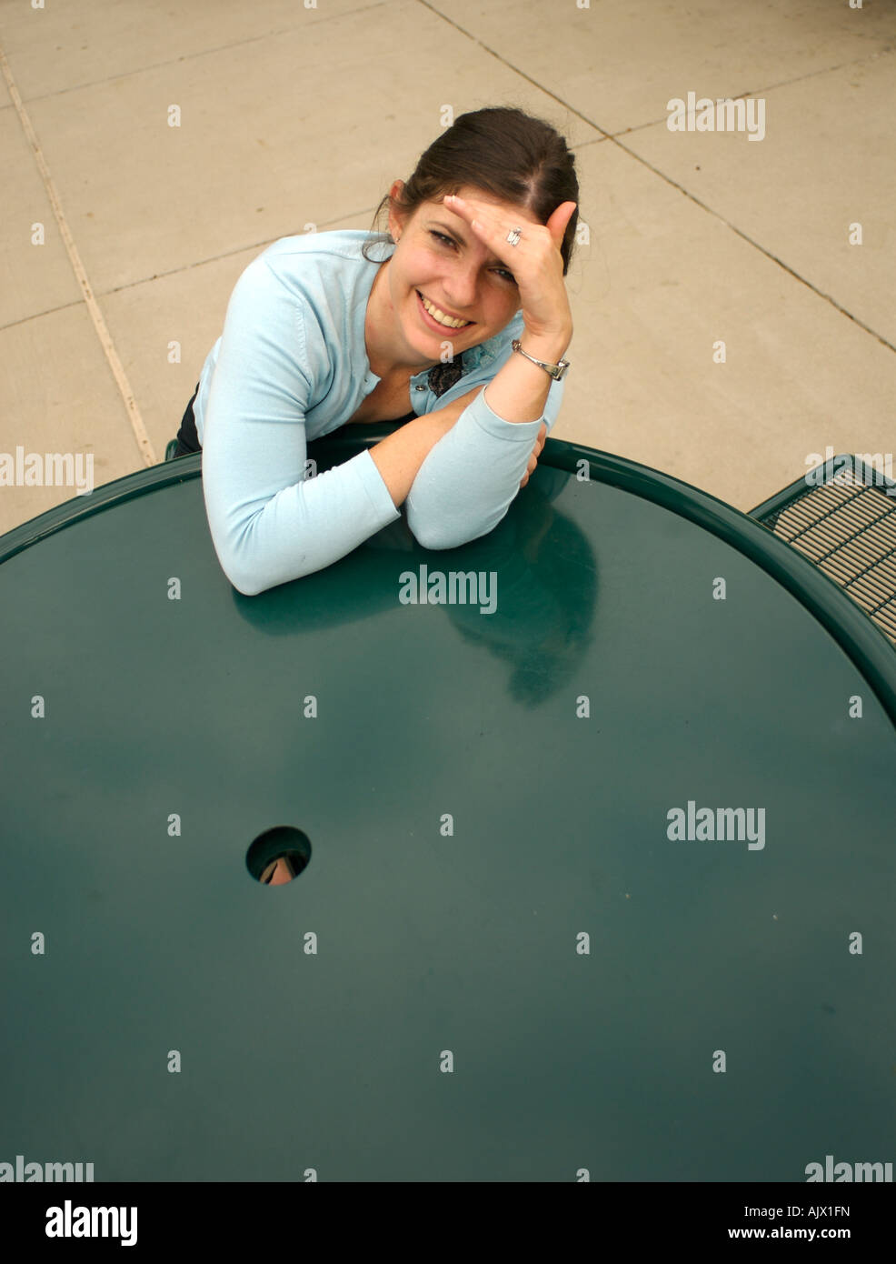 Young woman sitting at a green table looking up and shading her eyes ...