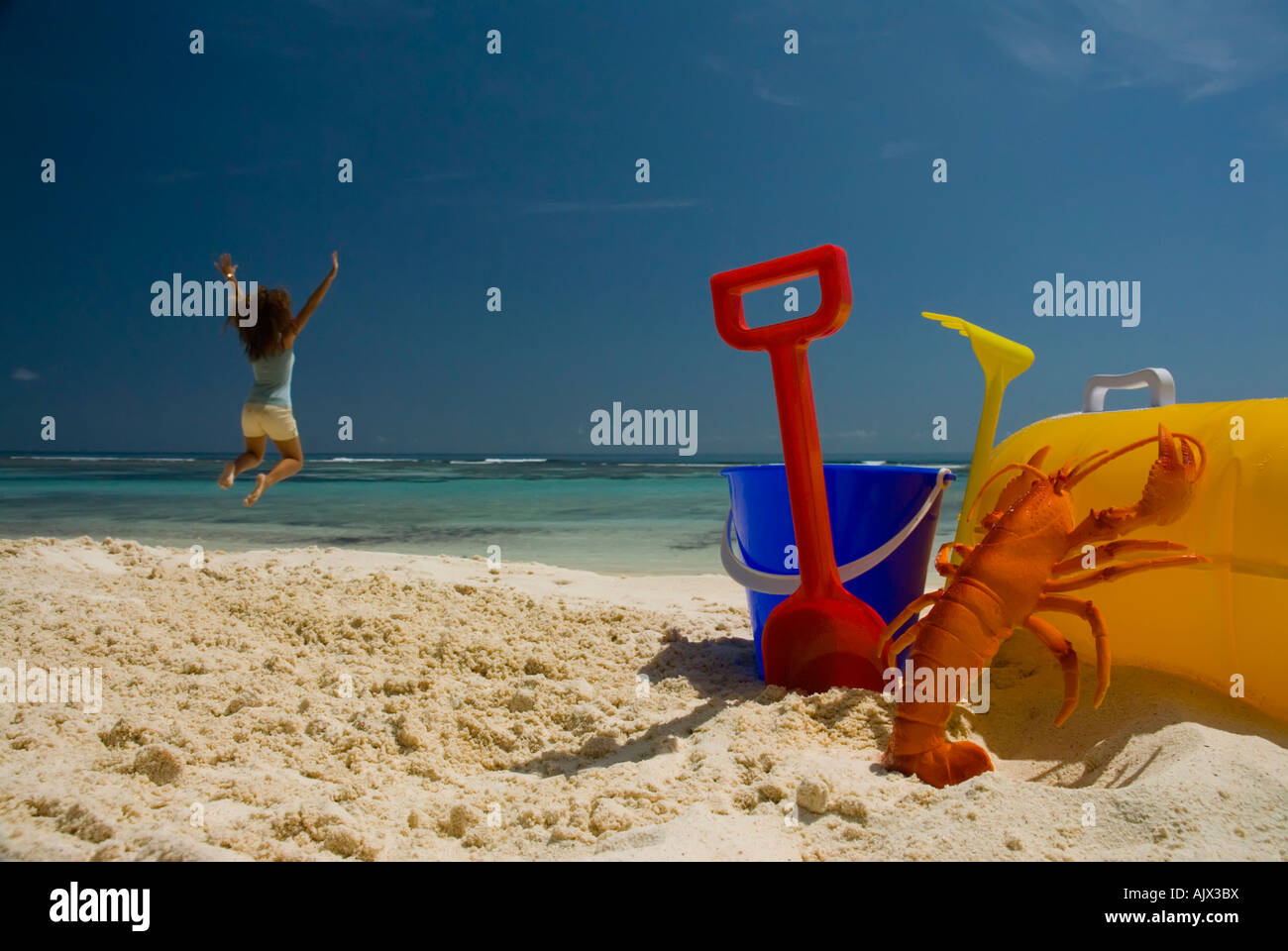Girl jumping for joy on tropical white sandy beach with beach toys in ...