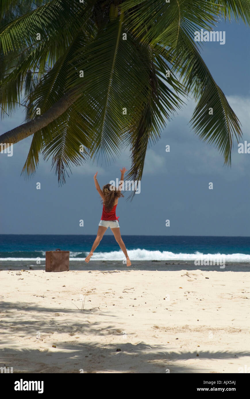 Girl stretching out jumping on white sandy tropical beach with suitcase ...