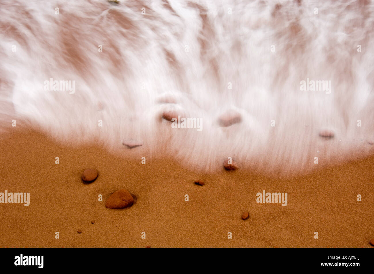 Beach sand and red rocks with incoming light surf runoff patterns ...