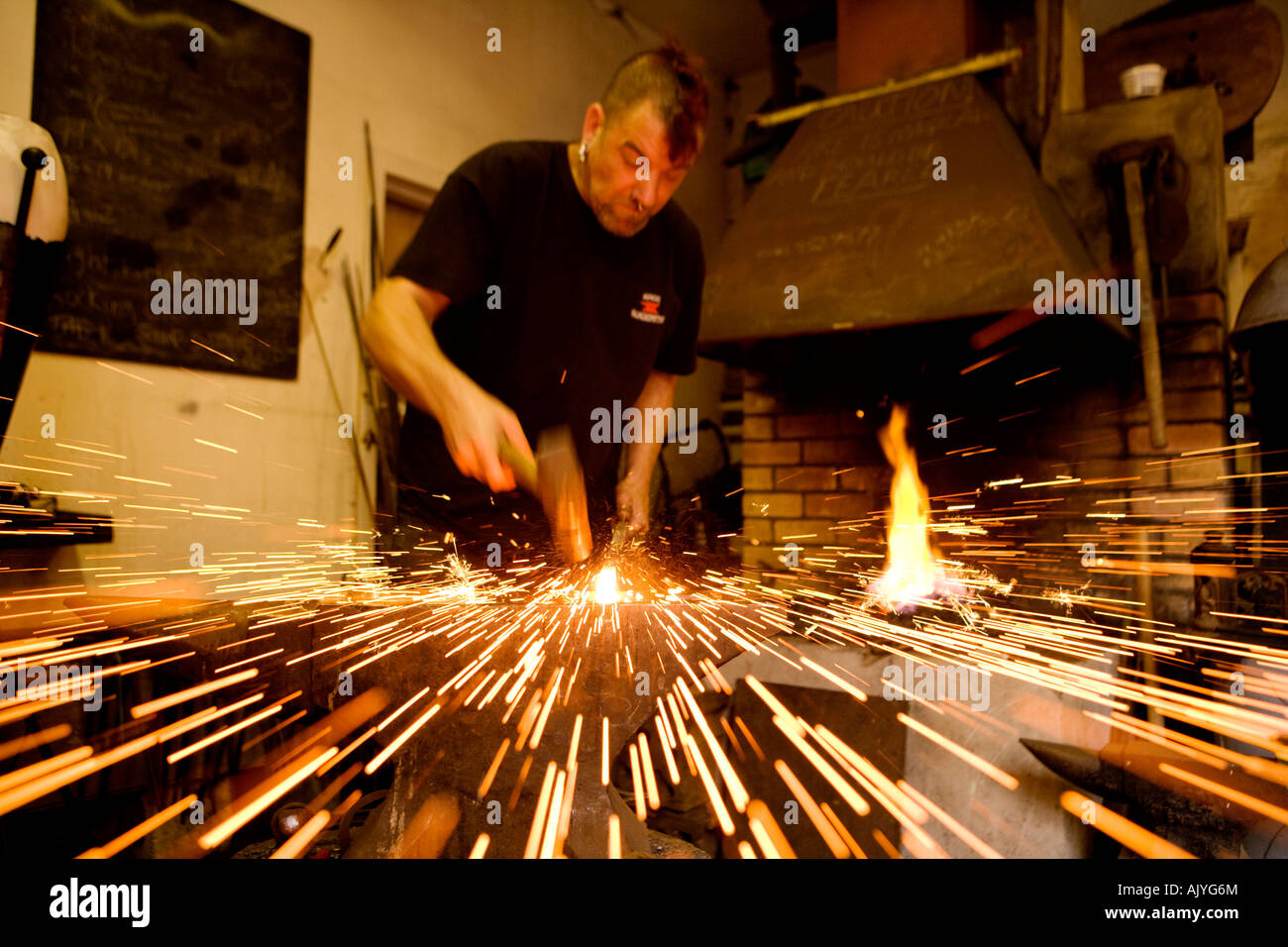 Blacksmith hammering red hot metal on an anvil with sparks fly off in ...