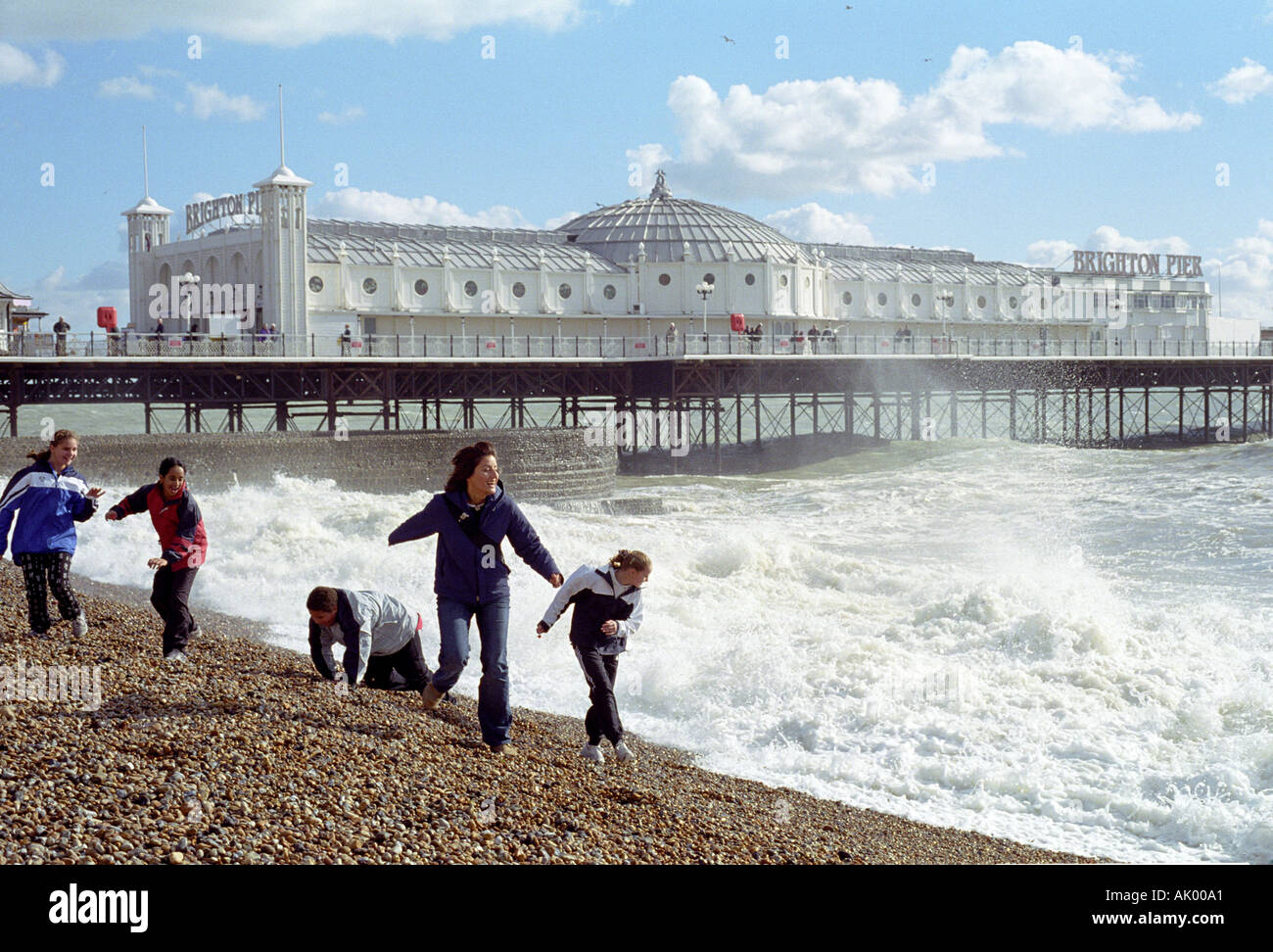 People running from the waves on the beach with the Brighton pier in ...