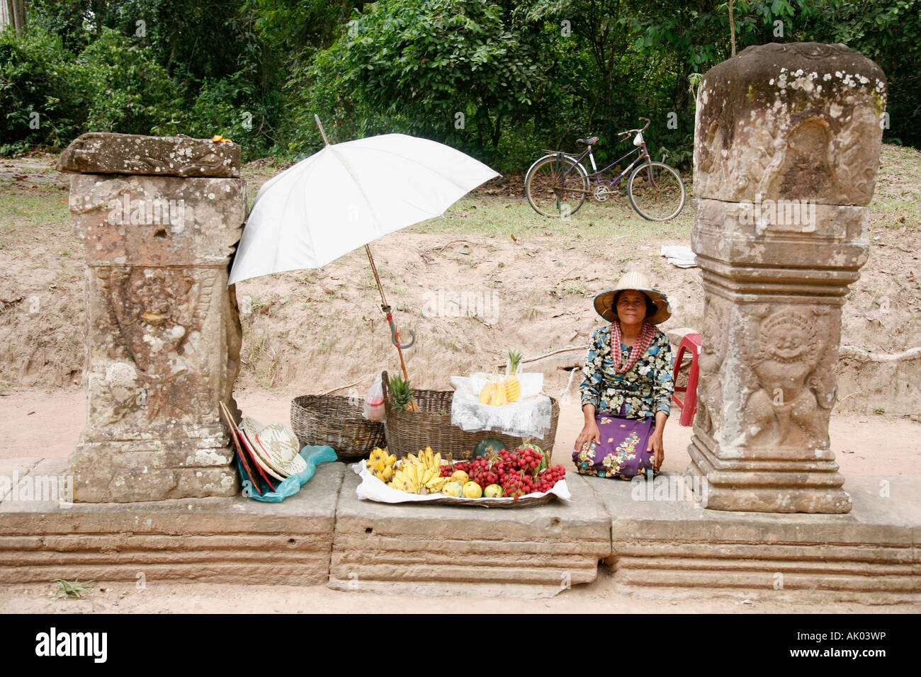 A woman with a bicycle and umbrella selling fruit inside of the Angkor ...