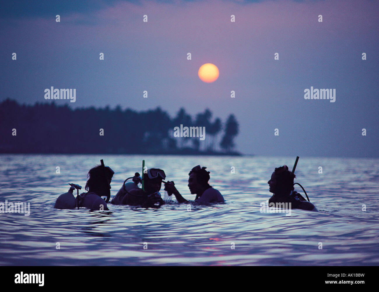 Indonesia. Group of scuba divers silhouetted against tropical headland ...