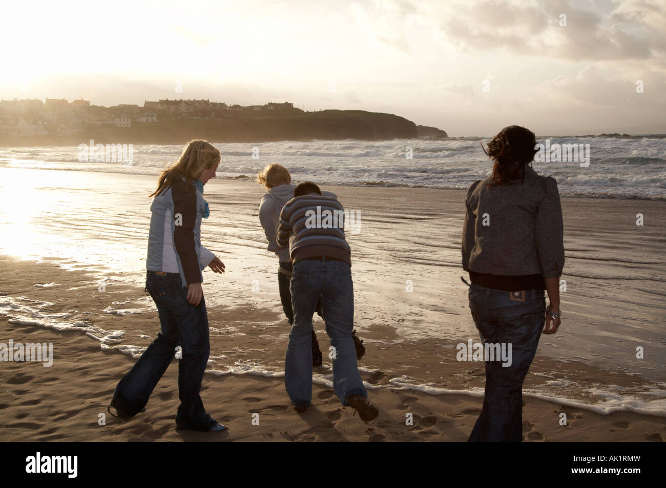 group of teenage student friends messing about on a beach at sunset ...