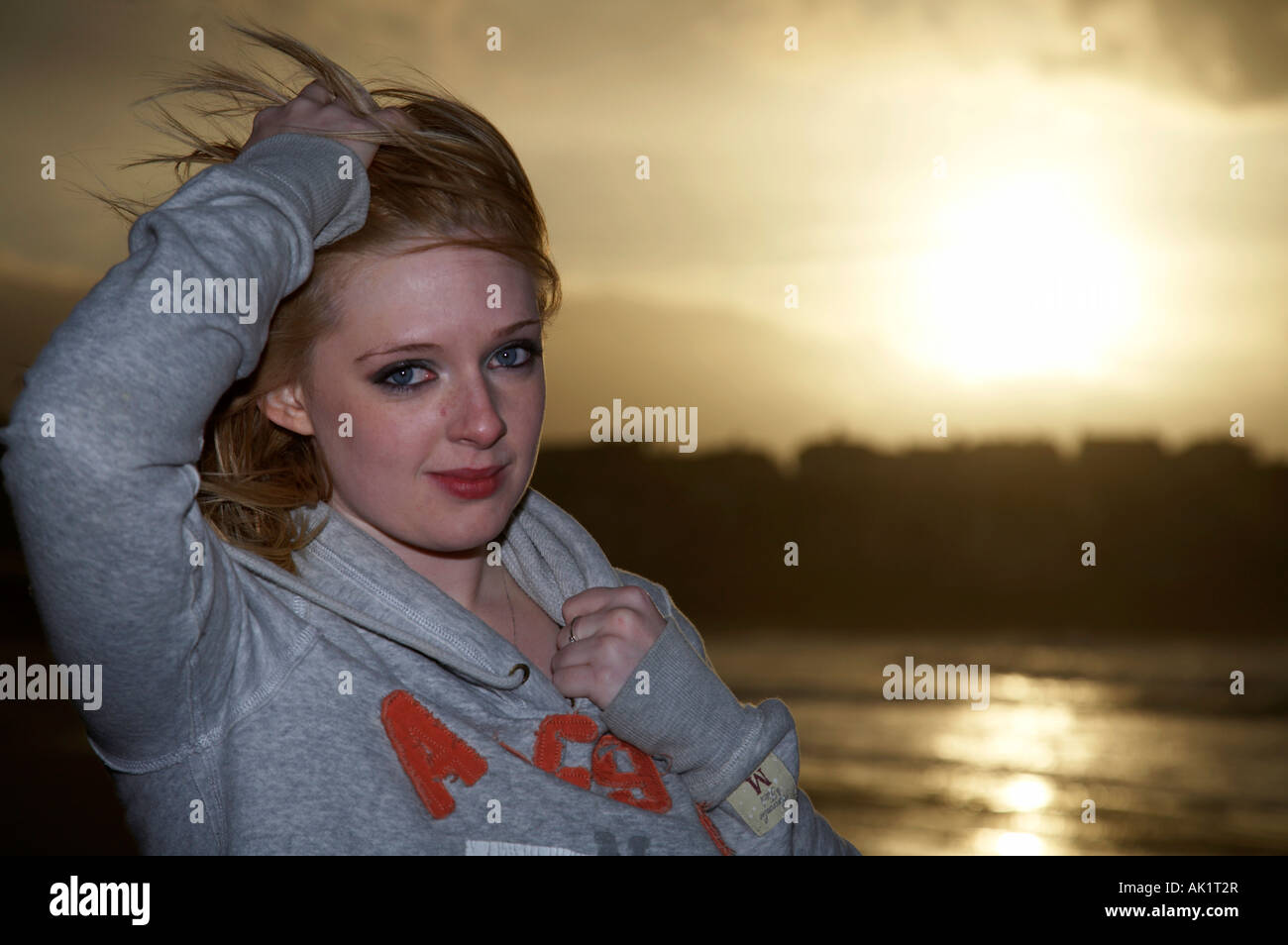 blonde haired female student standing on a beach at sunset looking ...
