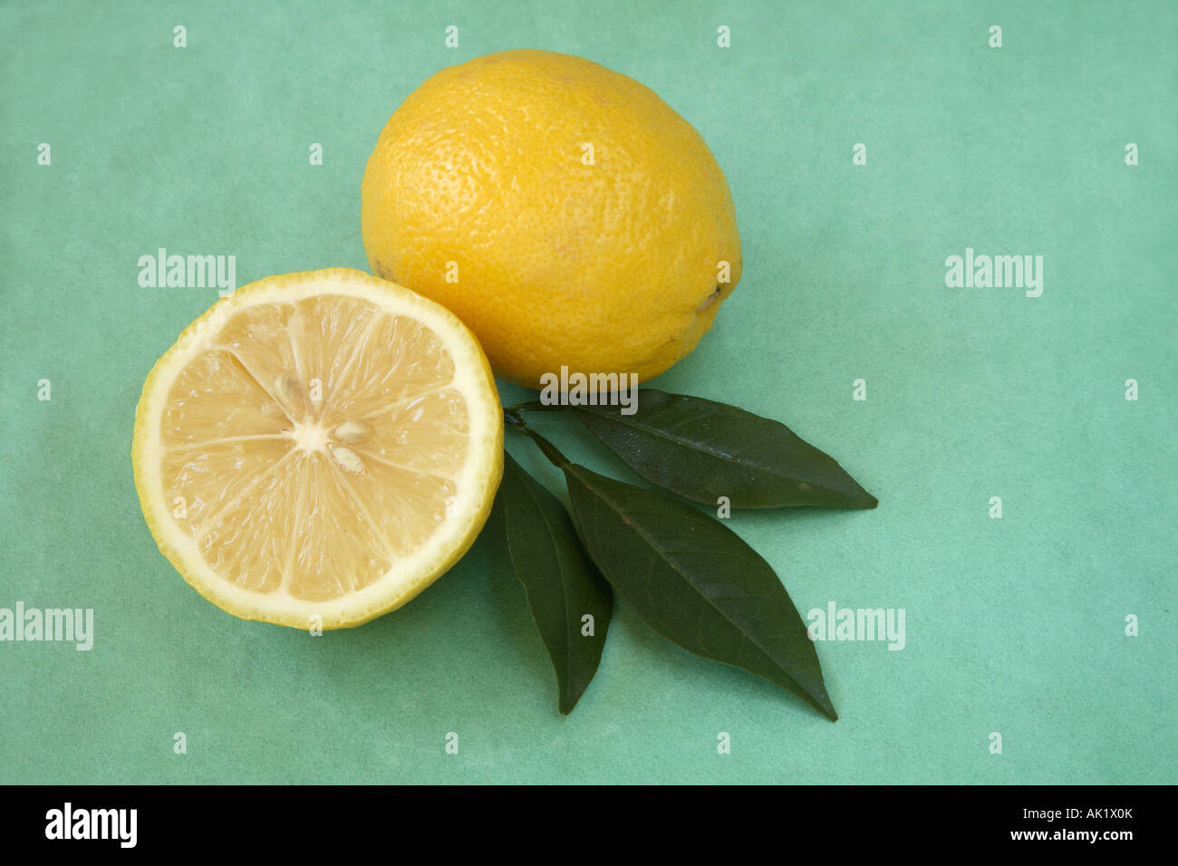 Whole lemon beside a half cut lemon with sprig of fresh lemon leaves in ...
