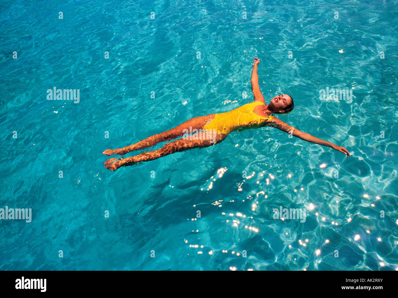 Maldives. Young woman in swimsuit floating on her back in clear water ...