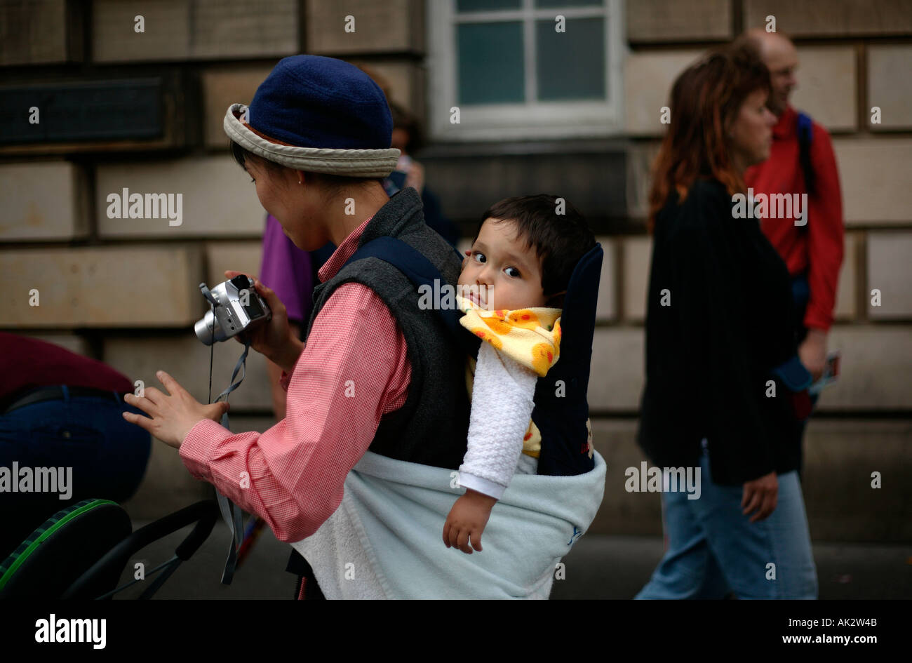Woman carrying baby on her back in a sling while looking at her digital ...