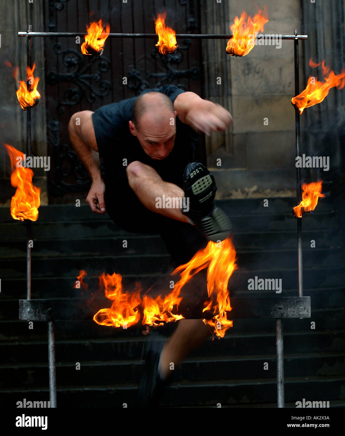 Male street performer leaping through metal frame surrounded by flames ...