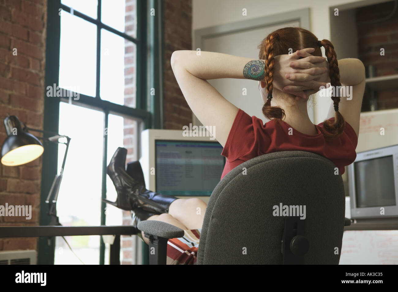 Red haired woman leaning back at her office desk Stock Photo - Alamy